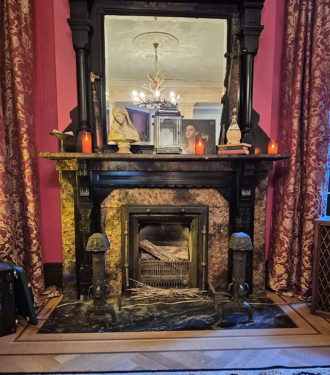 The fireplace mantel, adorned with candles and curiosities, serves as both functional hearth and shrine to the home's mysterious past.