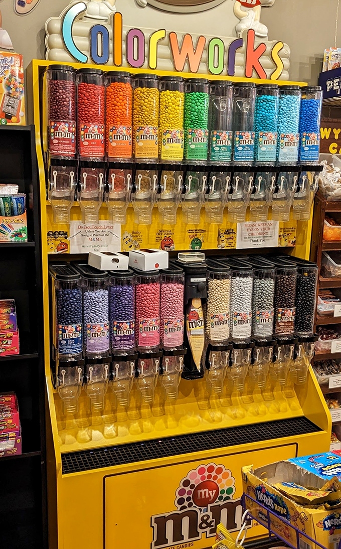 The M&M dispenser wall stands like a colorful apothecary, dispensing chocolate medicine for whatever ails you, one pull of the lever at a time.