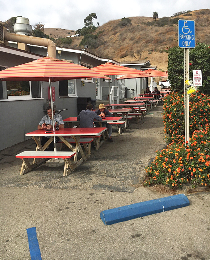 Red-topped picnic tables under orange umbrellas offer a casual spot to savor your seafood with Malibu hills as backdrop.