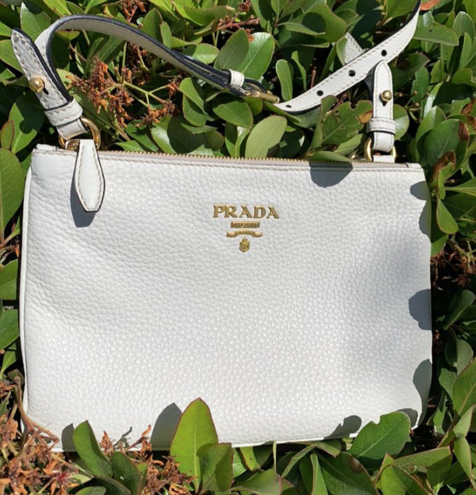This pristine white Prada bag lounges against greenery, a reminder that luxury and nature aren't mutually exclusive concepts.