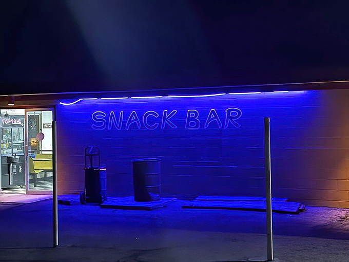The neon "SNACK BAR" sign glows electric blue against the night, a siren call for moviegoers craving intermission treats.