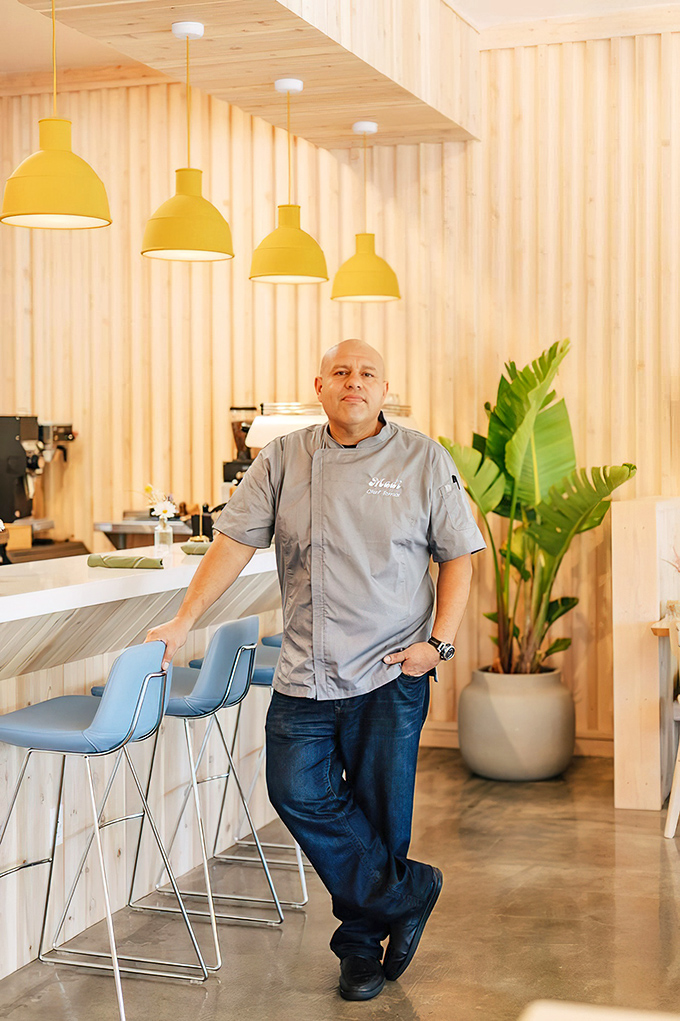 Yellow pendant lights hang like California sunshine, illuminating a space where wood slats and tropical plants create the perfect breakfast backdrop.