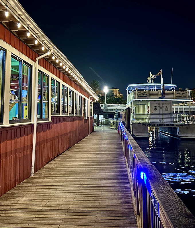 Evening transforms the waterfront deck into a string-lit paradise where dinner conversations flow as smoothly as the tide beneath the weathered boards.