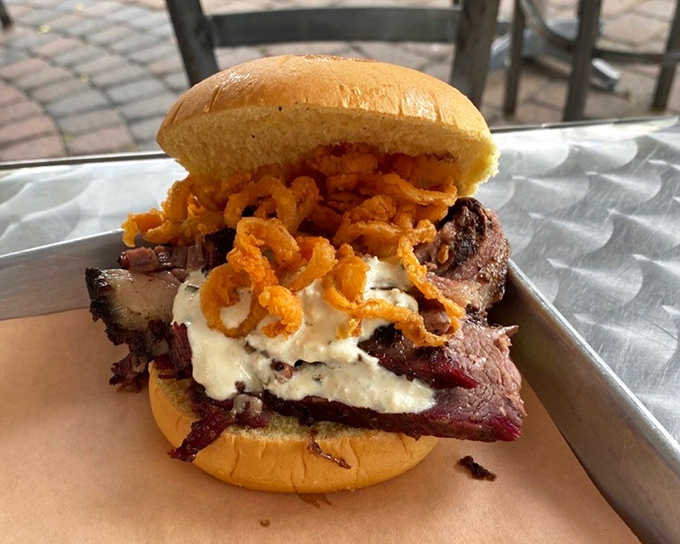 This sandwich defies gravity and good manners &ndash; stacked high with smoked meat, creamy topping, and crispy onions. A beautiful mess worth every napkin.