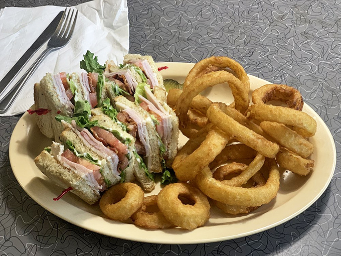A club sandwich that stands taller than some Arizona cacti, flanked by onion rings that could double as delicious golden halos.