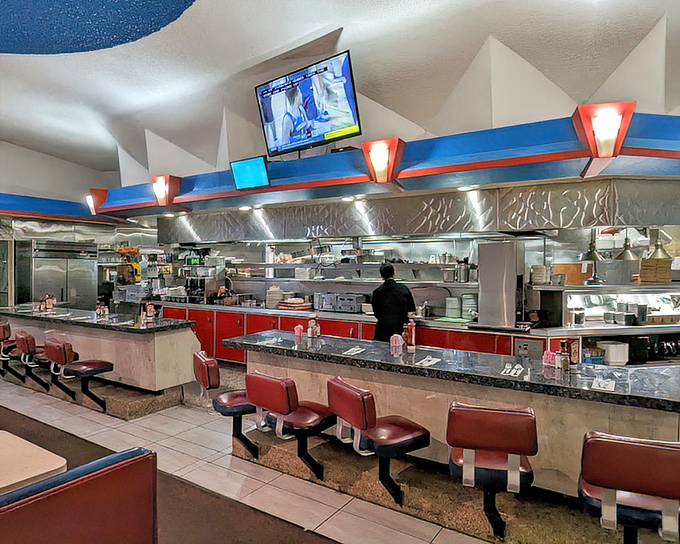The counter seating offers front-row tickets to the culinary show. Red accents pop against stainless steel in this classic diner setup.