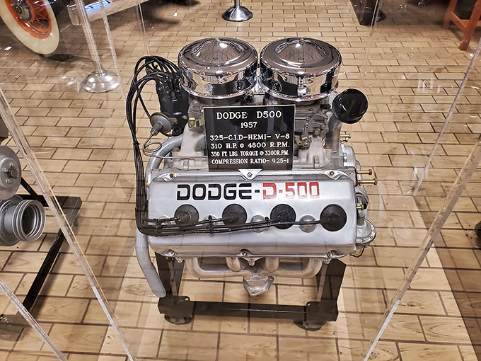 The 1957 Dodge D-500 engine gleams like jewelry in its display case. This 310-horsepower heart once pumped pure American muscle down the strip.