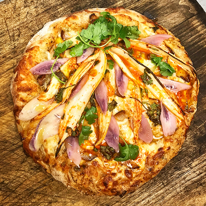 This pizza looks like it dressed up for a special occasion, with purple onions and fresh herbs adding pops of color to the golden canvas.