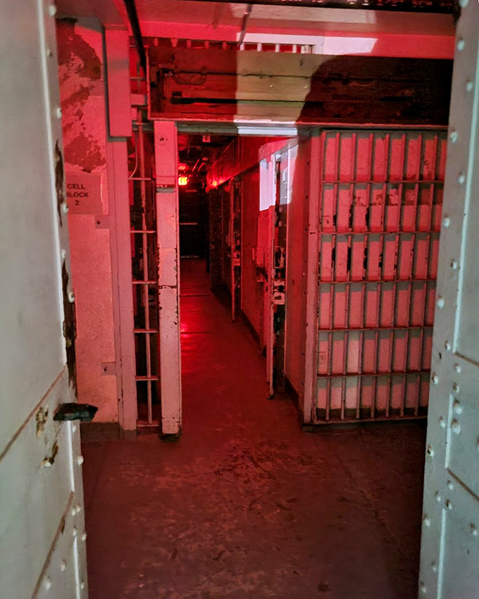 The eerie red glow of modern lighting creates an atmospheric backdrop for "Cell Block 2," highlighting the claustrophobic conditions inmates once endured.