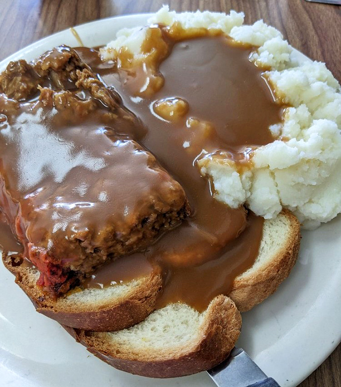 Open-faced meatloaf sandwich swimming in gravy&mdash;comfort food that doesn't need a therapist's license. That mashed potato dam holding back the gravy river deserves an engineering award.