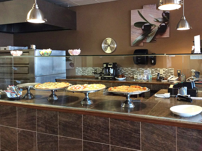 Behind the counter, where pizza dreams come true on silver pedestals, waiting for their moment in the spotlight of your dinner table.