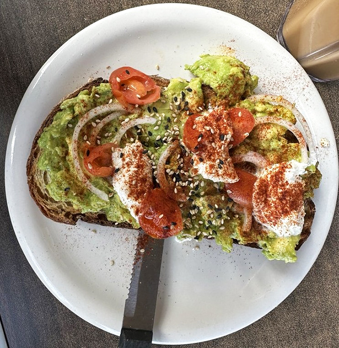 Avocado toast that transcends basic status with thoughtful additions of sesame seeds, paprika, and perfectly ripe tomatoes.
