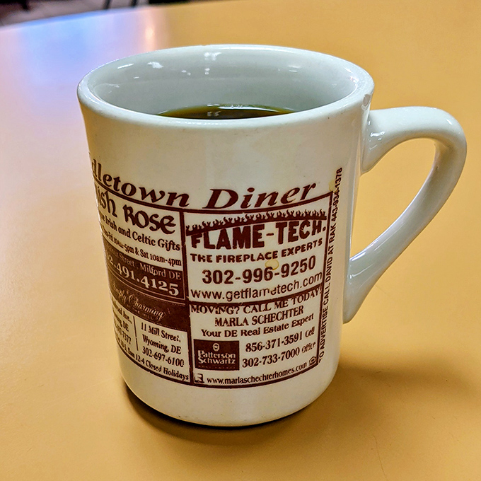 The coffee mug doubles as local advertising and conversation starter. In diners like this, a good cup of joe comes with a side of community connection.