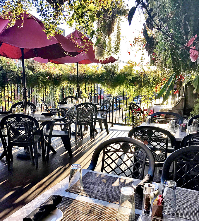 Dappled sunlight filters through the outdoor dining area, where red umbrellas stand guard over tables set for afternoon conversations and evening romances.