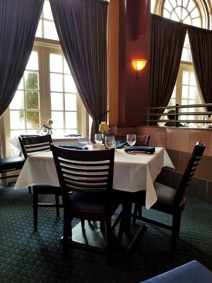 Elegant simplicity: white tablecloths, dark wood chairs, and dramatic drapes frame tall windows that let natural light dance across your dining experience.