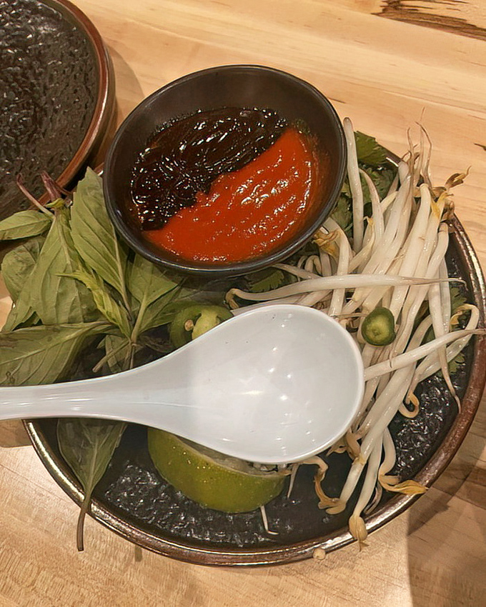 The pho accompaniments arrive like supporting actors ready for their big scene&mdash;fresh herbs, bean sprouts, and sauces waiting for their cue.
