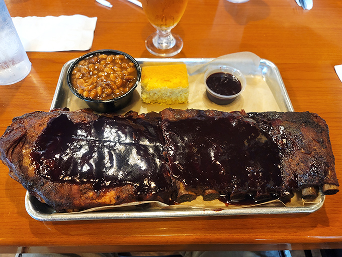 Ribs glazed with sauce that glistens like edible stained glass, accompanied by beans and cornbread for the full experience.