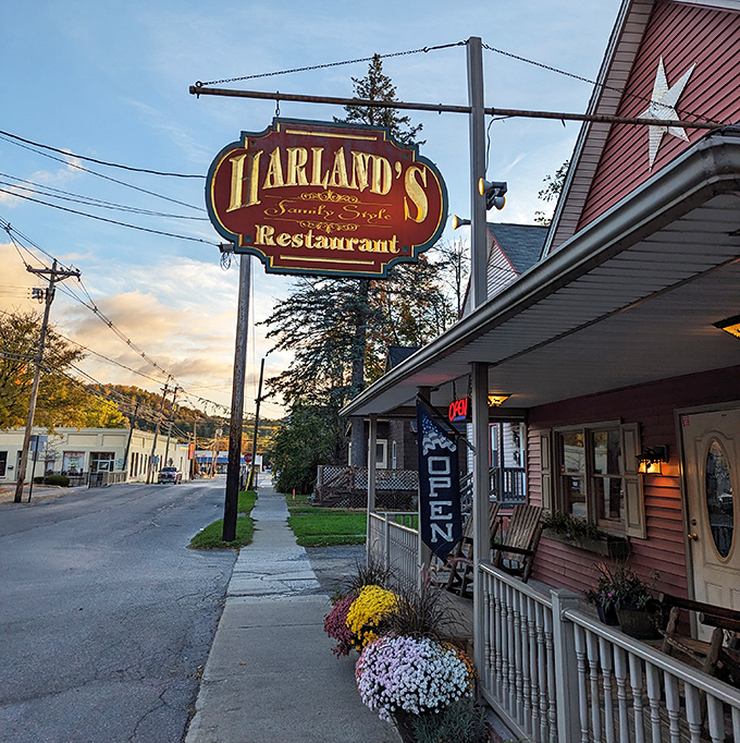 Harland's Restaurant sign swings above flower-lined steps, a beacon for hungry travelers seeking authentic small-town dining experiences.