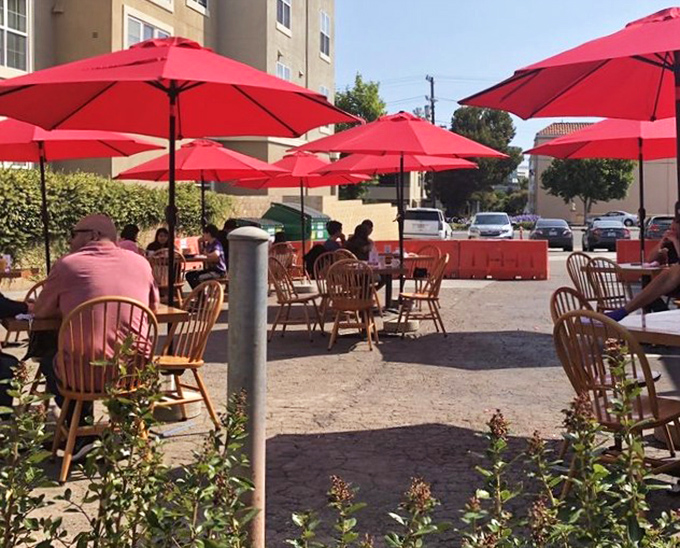 Outdoor dining under cherry-red umbrellas &ndash; California sunshine and pancakes proving that some combinations are simply unbeatable.