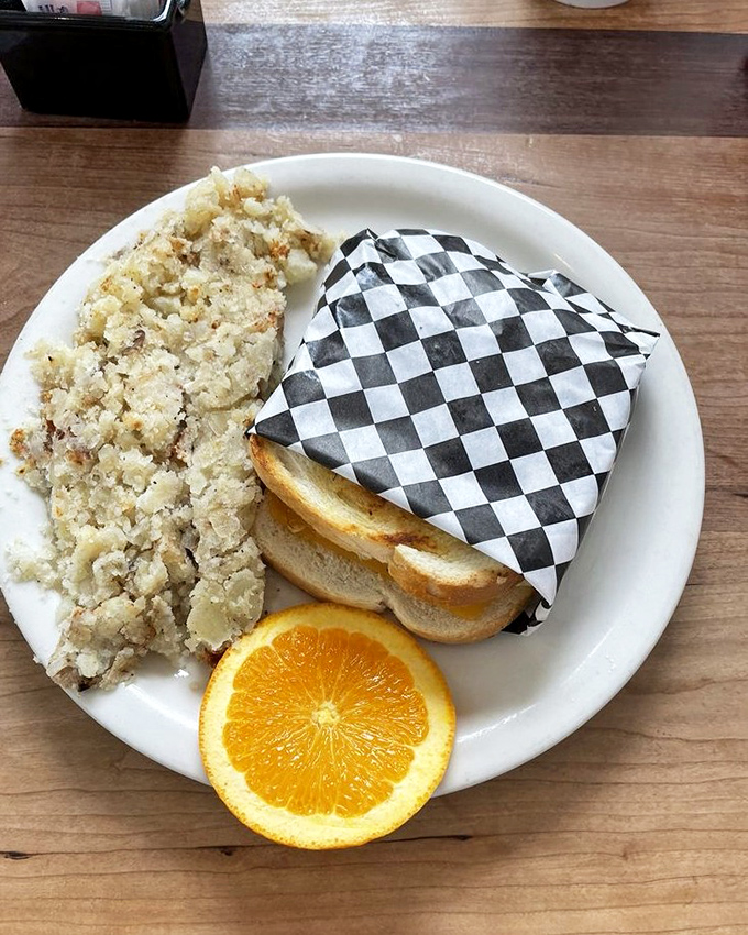The perfect partnership &ndash; a sandwich wrapped in checkered paper alongside hash browns and a bright orange slice for a pop of color.