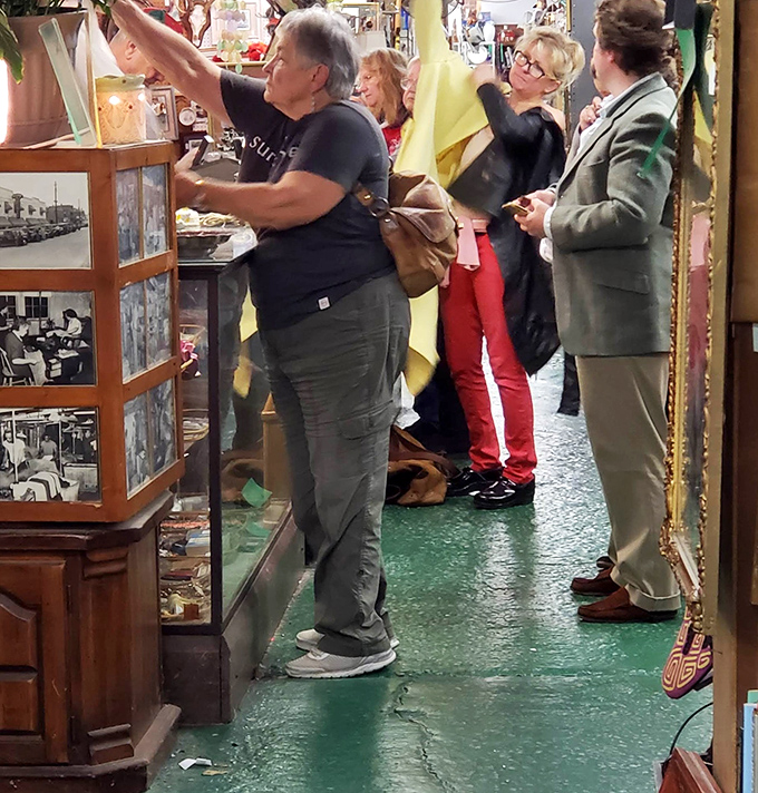 Treasure hunters in their natural habitat, reaching for history while surrounded by it. That green floor has supported more antique enthusiasts than a PBS fundraiser.