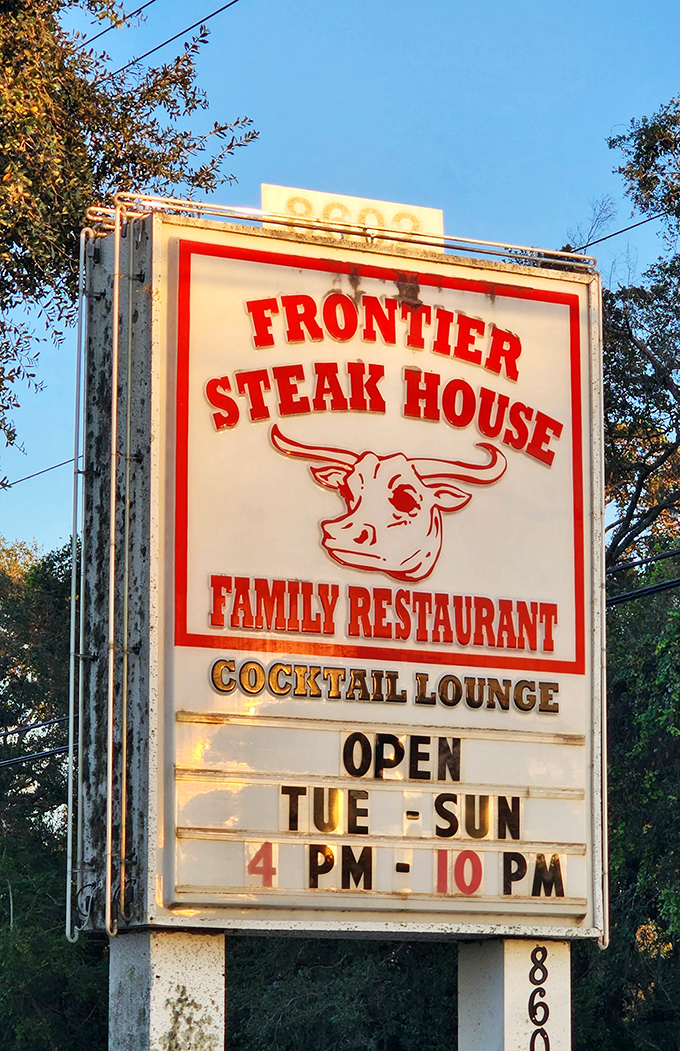 The roadside sign beckons like a meaty lighthouse, guiding hungry travelers to the promised land of perfectly grilled steaks and cold cocktails.