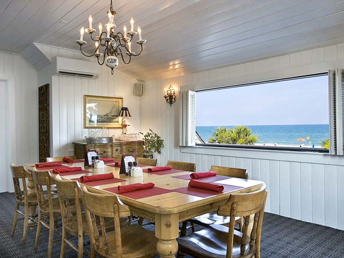 The upstairs dining room combines elegance with coastal casualness&mdash;white-paneled walls, wooden tables, and that picture window framing the Atlantic like a living painting.