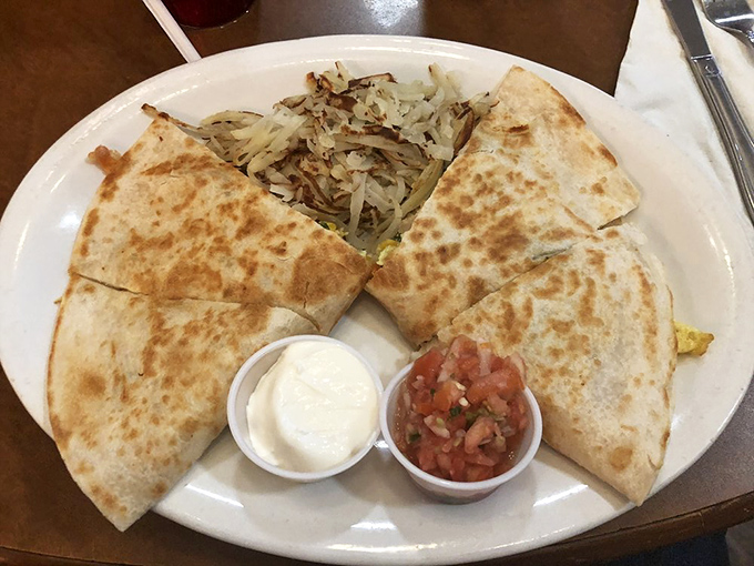 Quesadilla cut with geometric precision, revealing its melty secrets. The perfect ratio of crisp exterior to gooey interior, with salsa and sour cream standing by.
