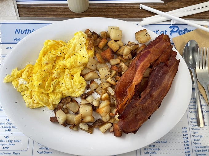 The breakfast trinity: fluffy scrambled eggs, golden home fries, and bacon cooked to that perfect point between chewy and crisp. Simple perfection on a white plate.