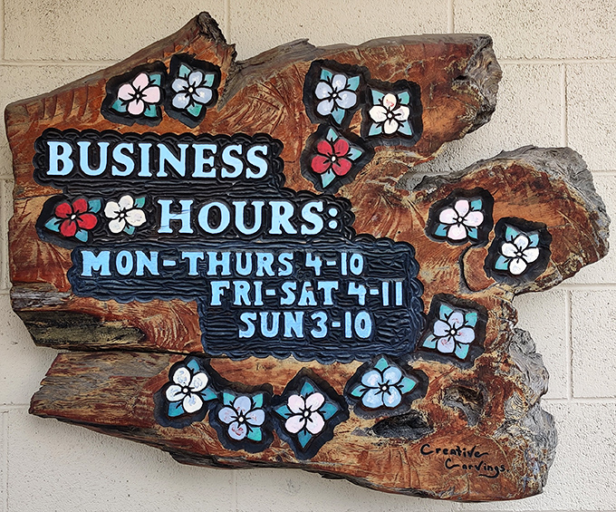 Business hours carved into wood with flower accents – practical information delivered with unexpected artistry.