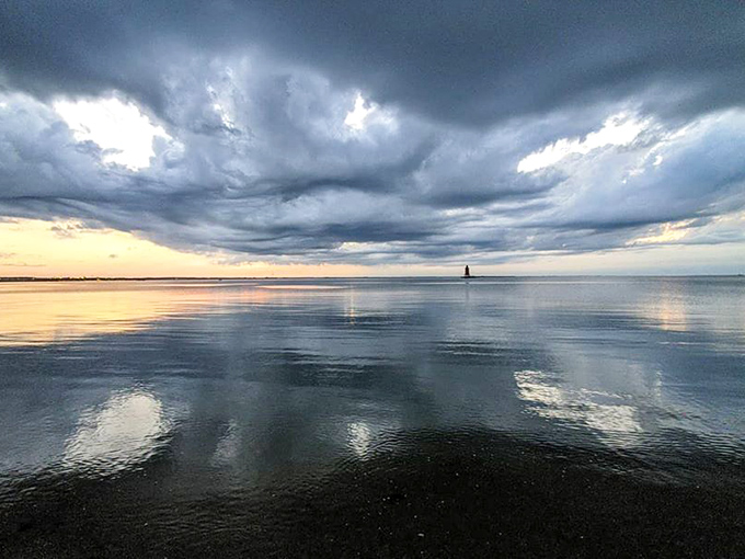 Dramatic skies reflect perfectly in still waters, creating nature's most impressive mirror. The lighthouse adds just the right punctuation mark.