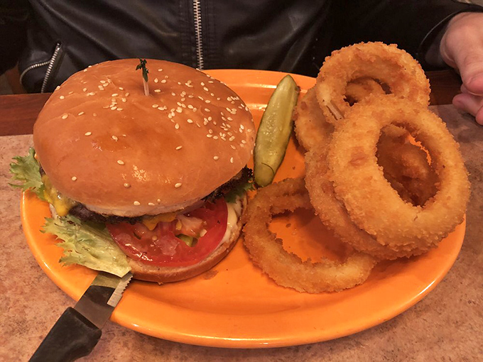 The burger and onion ring combo that makes you question why anyone would ever choose a salad, served on an orange plate that somehow makes everything taste better.
