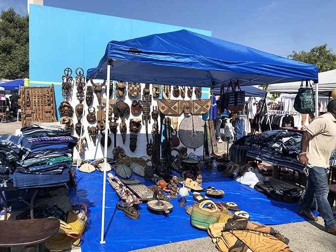 African masks and handcrafted treasures transform a simple blue tarp into a global bazaar worthy of extended browsing time.