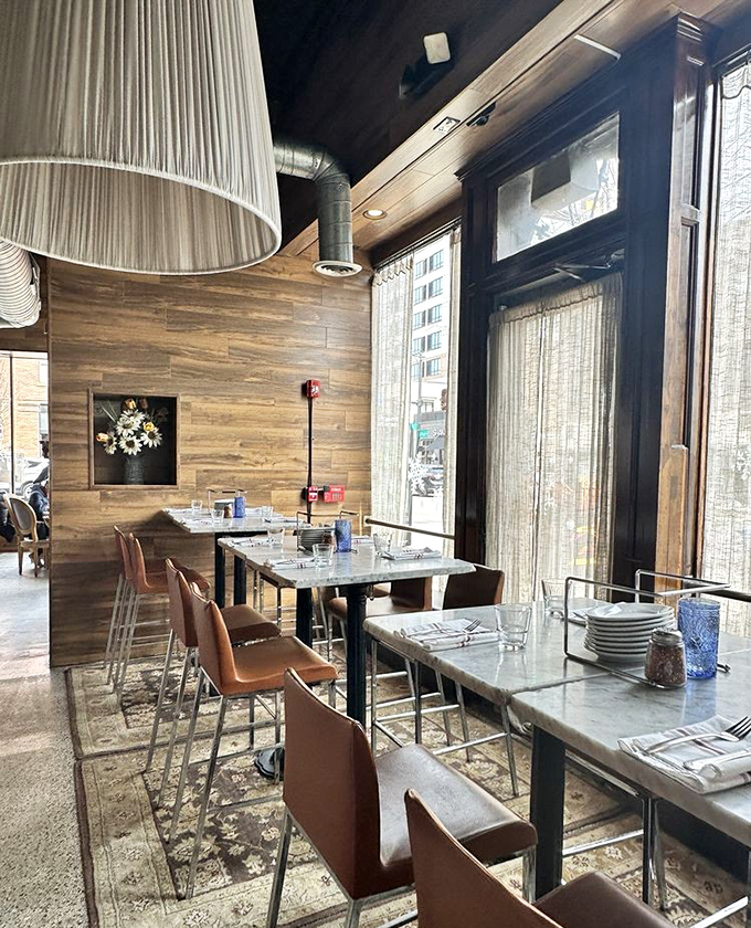 Natural light floods the dining area, highlighting marble tabletops and warm wood accents. The kind of space that makes Tuesday lunch feel like Saturday dinner.
