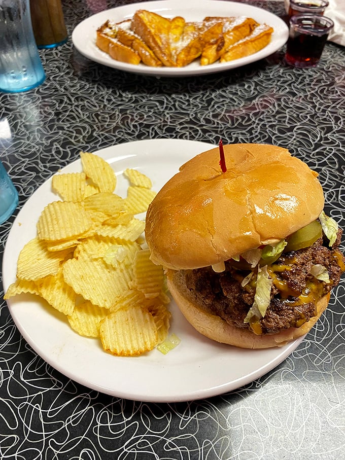 The cheeseburger in its natural habitat—surrounded by chips, with French toast lurking in the background. A balanced diet is a burger in each hand.