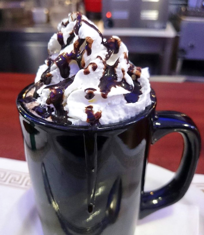 Hot chocolate elevated to an art form&mdash;whipped cream mountain drizzled with chocolate syrup. This isn't just a beverage; it's dessert with morning privileges.