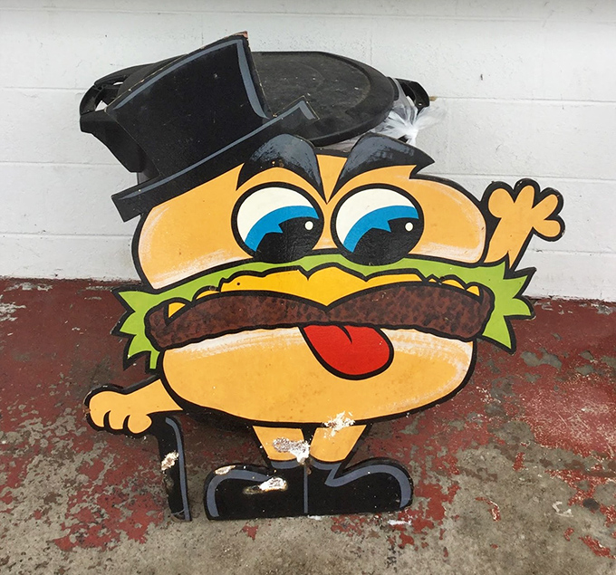 The burger mascot stands guard, a whimsical sentinel with a top hat and attitude, silently promising satisfaction to all who enter.