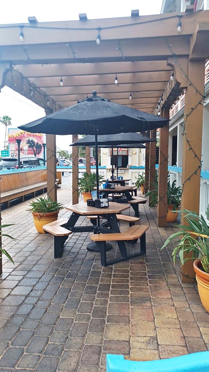 The outdoor patio offers string lights, umbrella-shaded tables, and potted palms &ndash; a casual oasis where beach vibes meet culinary delights.
