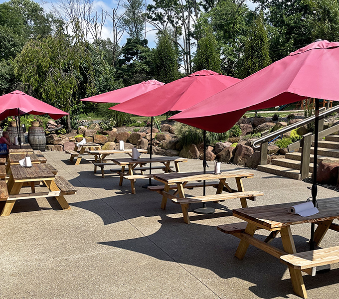 Outdoor seating under cherry-red umbrellas &ndash; nature's dining room with shade management. Pennsylvania summers were made for this.