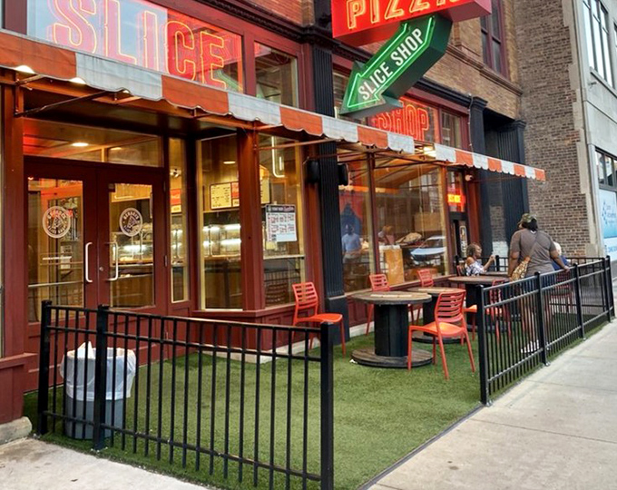 The outdoor patio's artificial turf and red chairs create an urban oasis where pizza tastes even better with a side of people-watching.