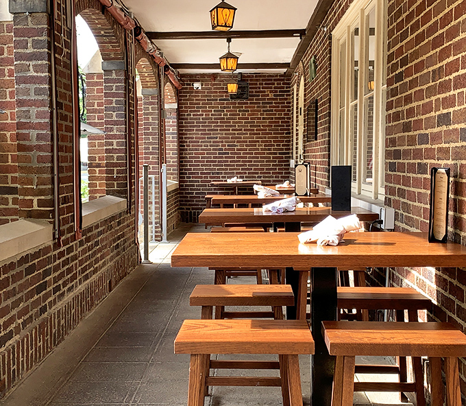 The covered patio offers a sheltered retreat where brick walls and wooden tables create an atmosphere of rustic European charm.