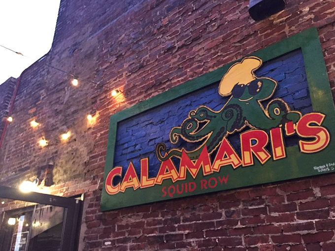 The Calamari's sign glows against brick like a beacon for hungry travelers, with that charming squid chef pointing the way to flavor town.