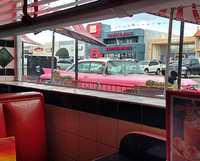 The view from inside: red vinyl booths frame the iconic pink Cadillac outside. Classic diner aesthetics with a dash of Arizona sunshine.