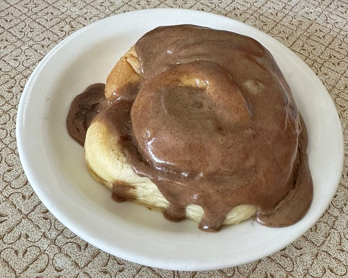 This cinnamon roll isn't just breakfast; it's a warm hug on a plate, draped in chocolate that melts away morning grumpiness with each bite.