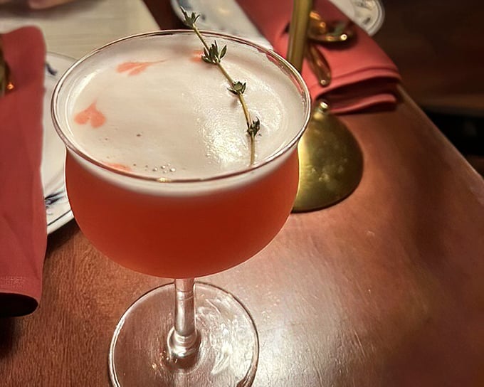 A pink cocktail garnished with fresh herbs that looks like it belongs in the hands of someone far cooler than you &ndash; until you order one yourself.