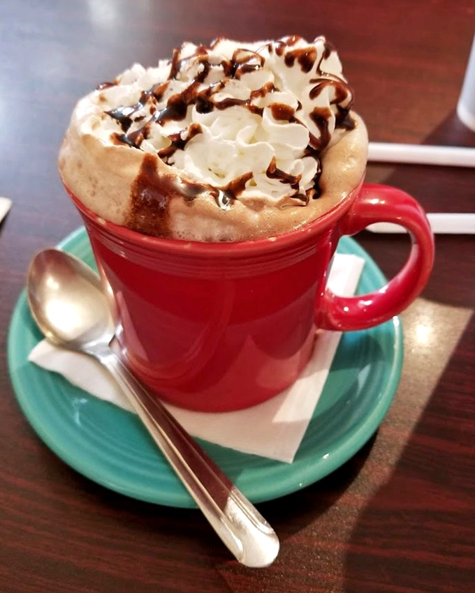 Hot chocolate crowned with whipped cream and chocolate drizzle&mdash;winter comfort in a cheerful red mug.