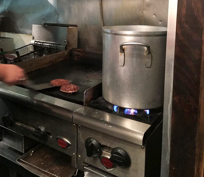 A glimpse into the kitchen reveals the no-nonsense approach to burger perfection—simple equipment, high heat, and skilled hands.