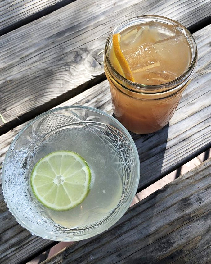 Two perfect companions for patio lounging—a crystal-clear cocktail with lime and its amber-hued cousin, both promising afternoon delight.