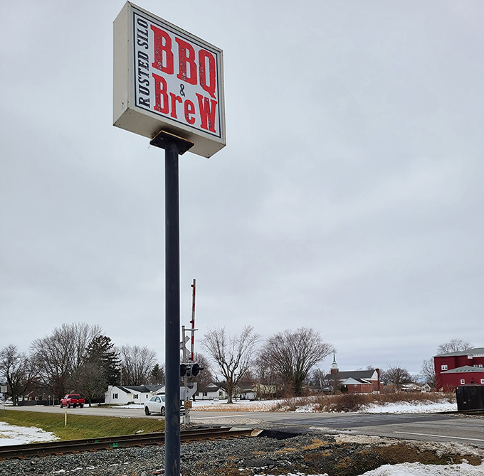 The modest roadside sign stands like a beacon of hope for hungry travelers, promising salvation in the form of perfectly smoked meats.