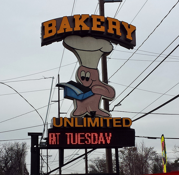This cheerful mascot sign announces "Hot Tuesday" like it's declaring a national holiday dedicated to fresh-baked happiness and community gathering.